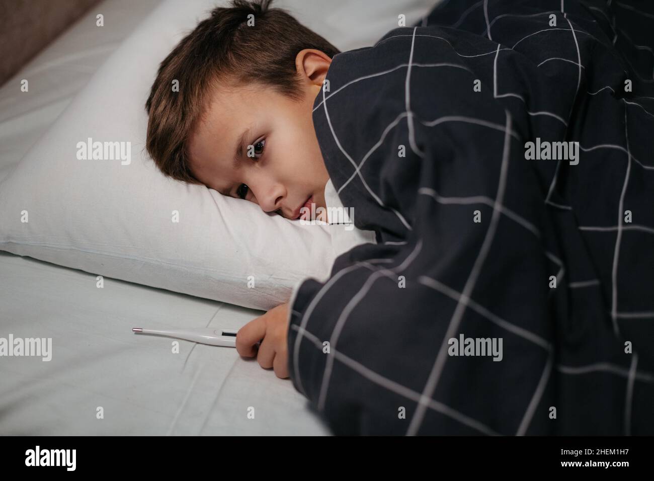 Sick child laying in bed and holding termometer Stock Photo - Alamy