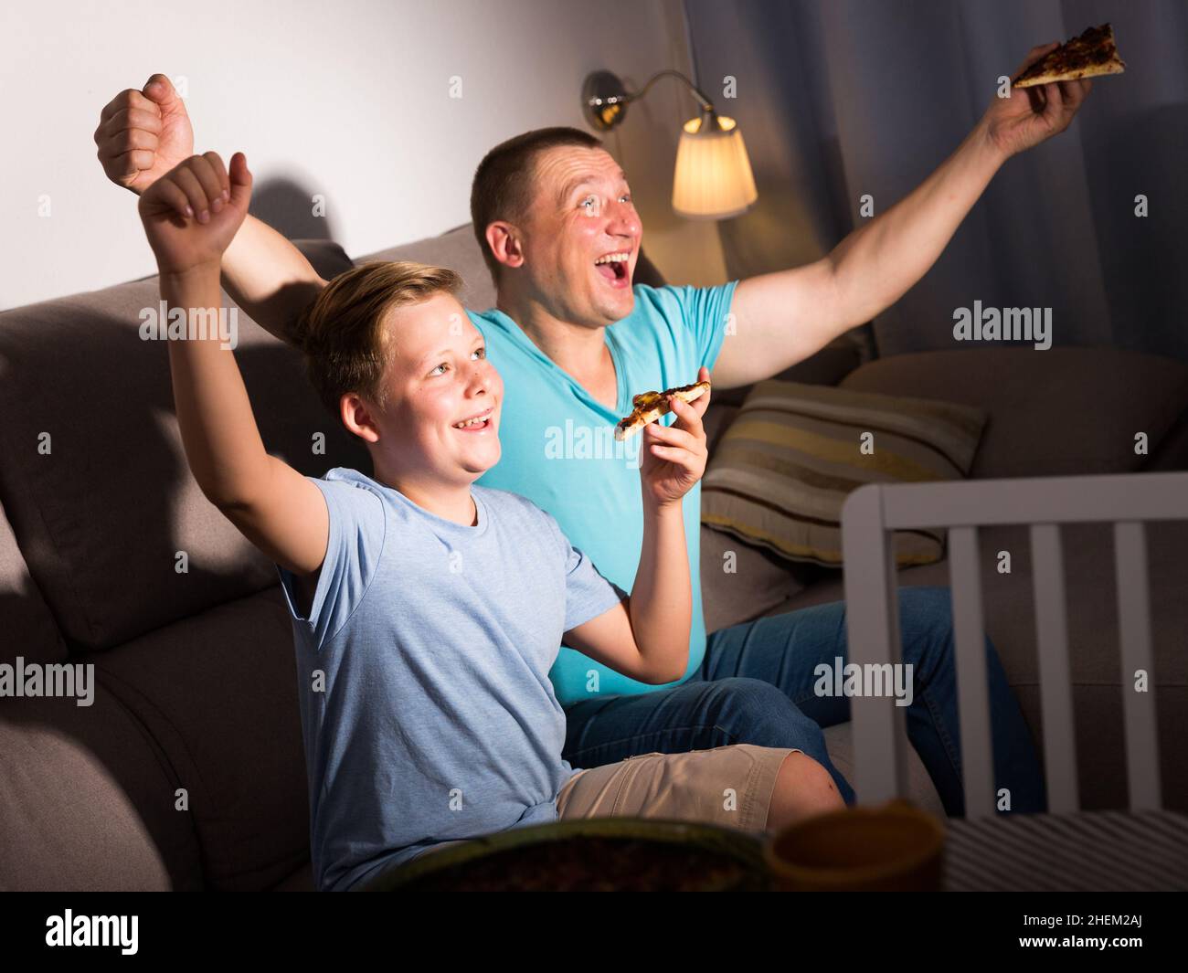 Smiling man is watching TV and cheering for football team with his son ...