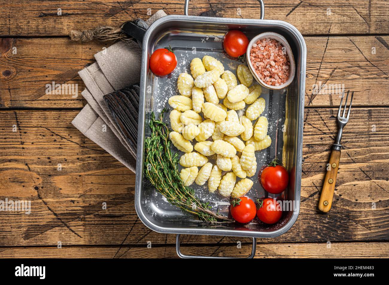 Uncooked Raw potato gnocchi in kitchen steel tray with herbs. Wooden ...