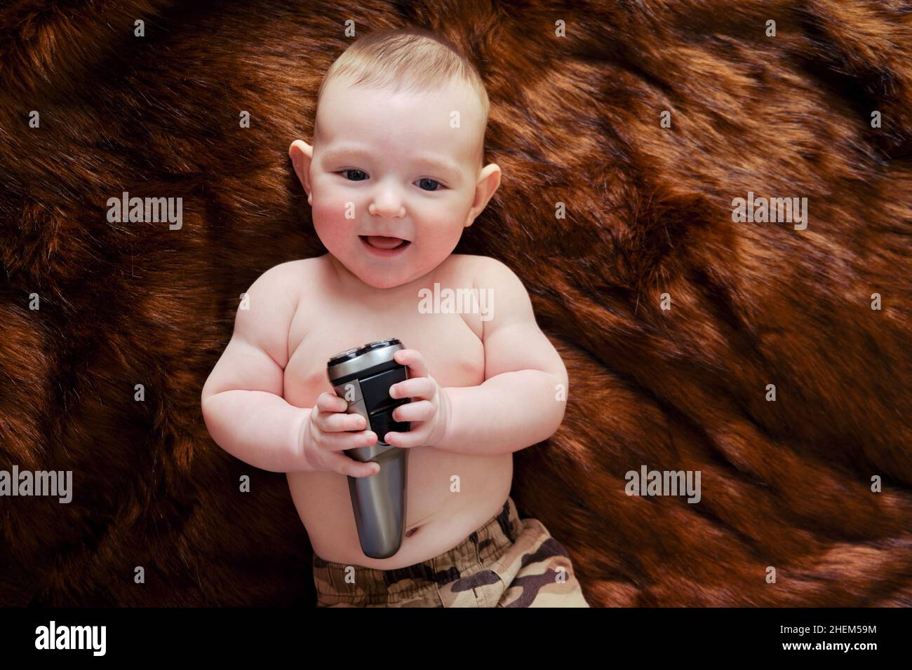 Funny happy baby boy with an electric shaver in his hands on a fur ...