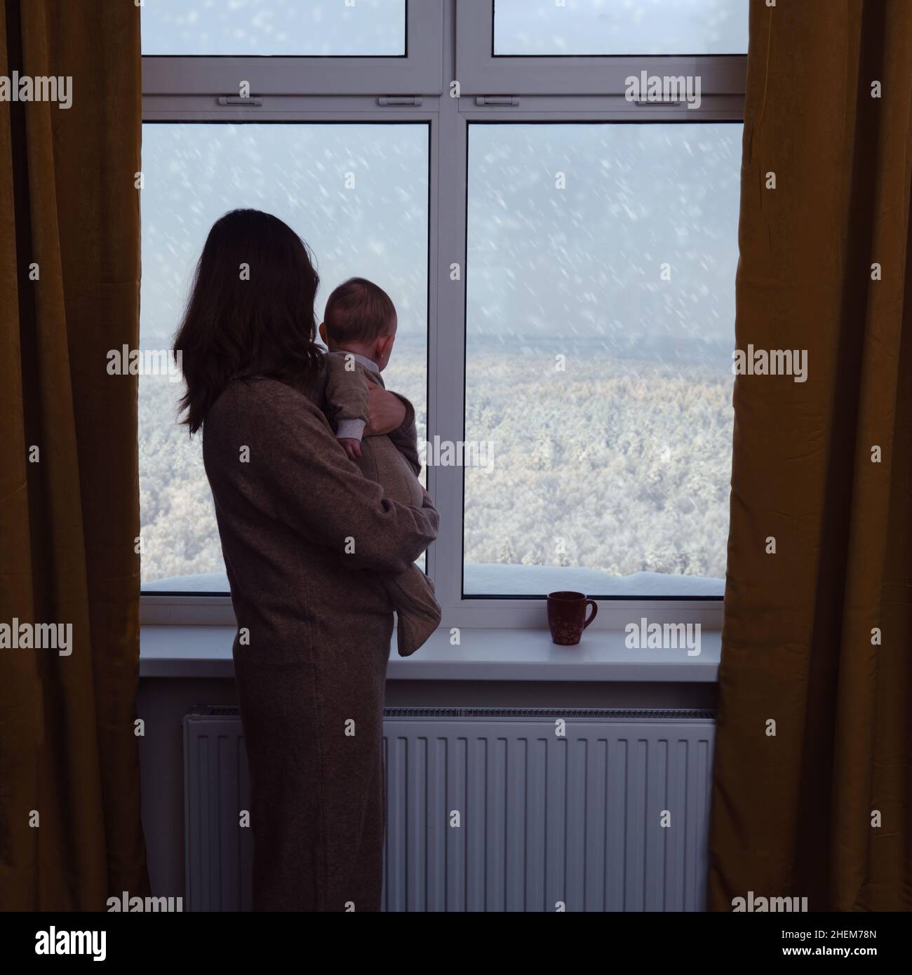 Snowfall outside the window and mom with baby in her arms. A mother ...