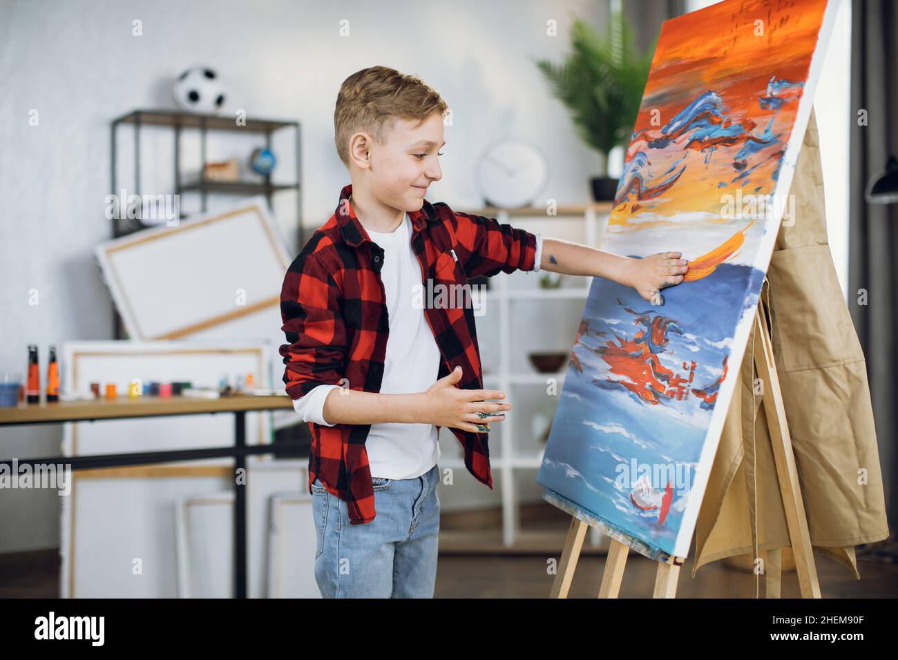 Happy caucasian boy in casual wear painting with hands on canvas during lesson at art school ...