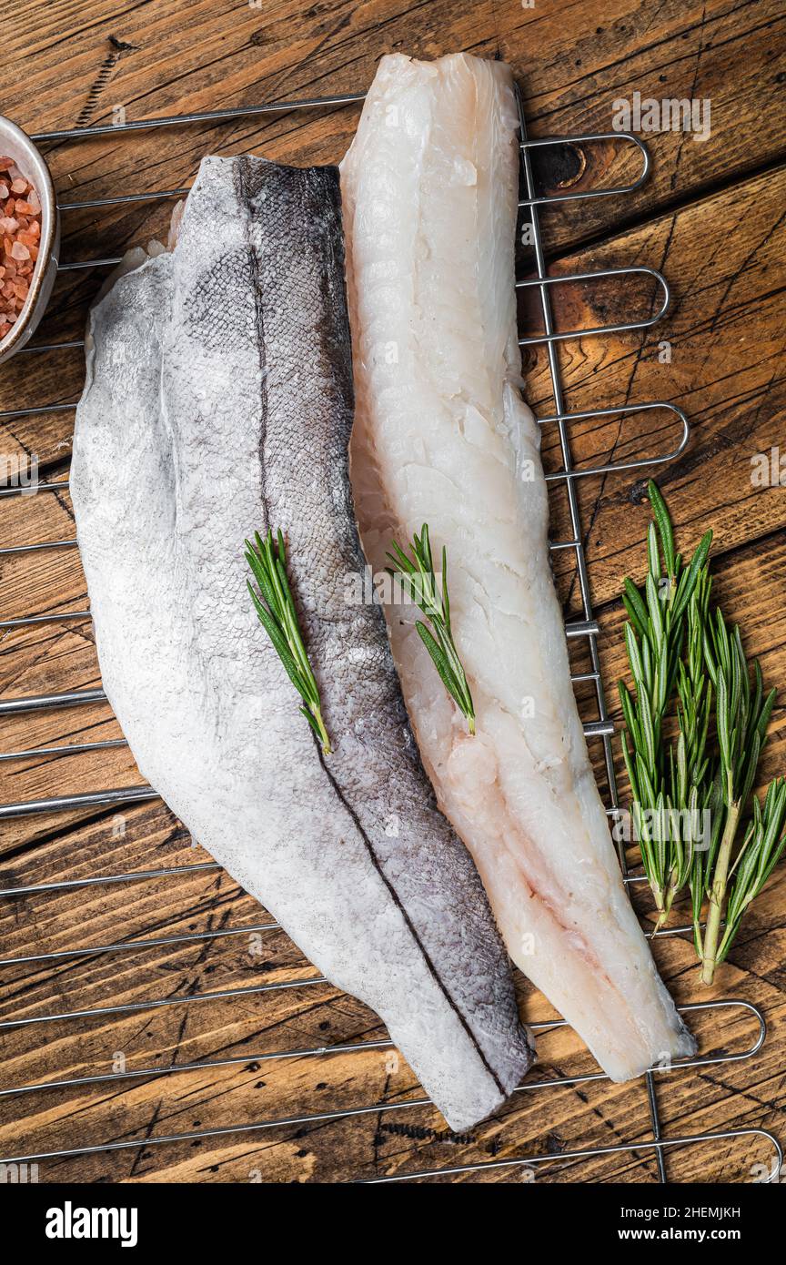Raw fish fillets on grill with rosemary and herbs. Wooden background ...