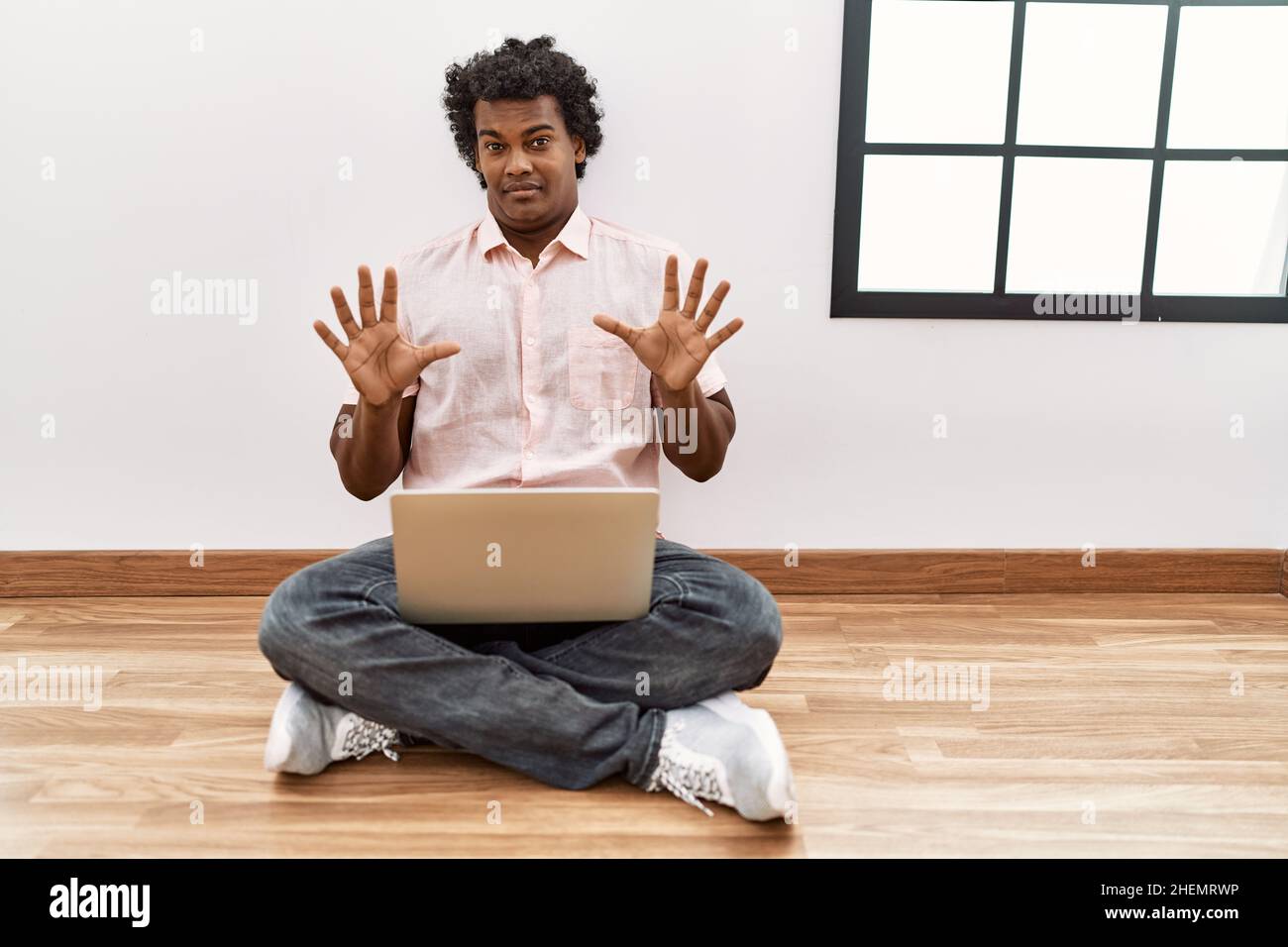 African man with curly hair using laptop sitting on the floor afraid ...
