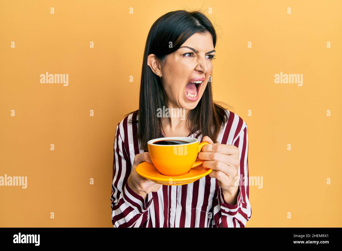 Young hispanic woman drinking a cup of coffee angry and mad screaming ...