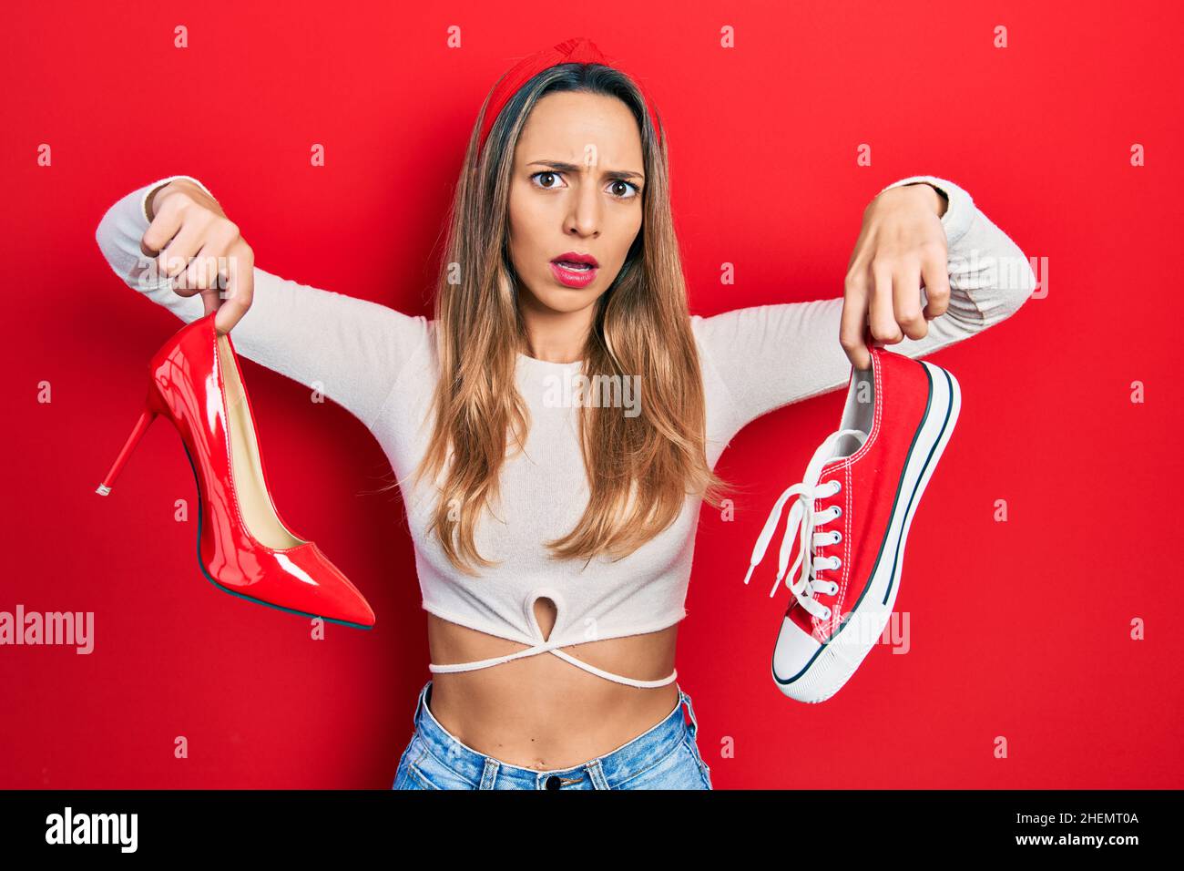 Beautiful hispanic woman choosing high heel shoes and sneakers in shock ...