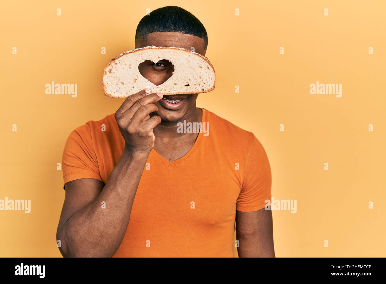 Young black man holding bread loaf with heart shape looking positive ...