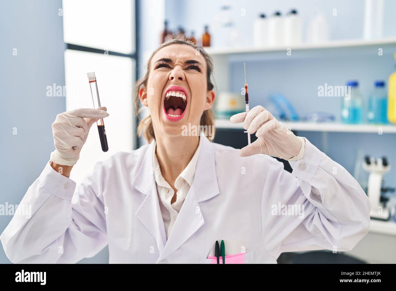Young woman working at scientist laboratory holding blood sample angry ...