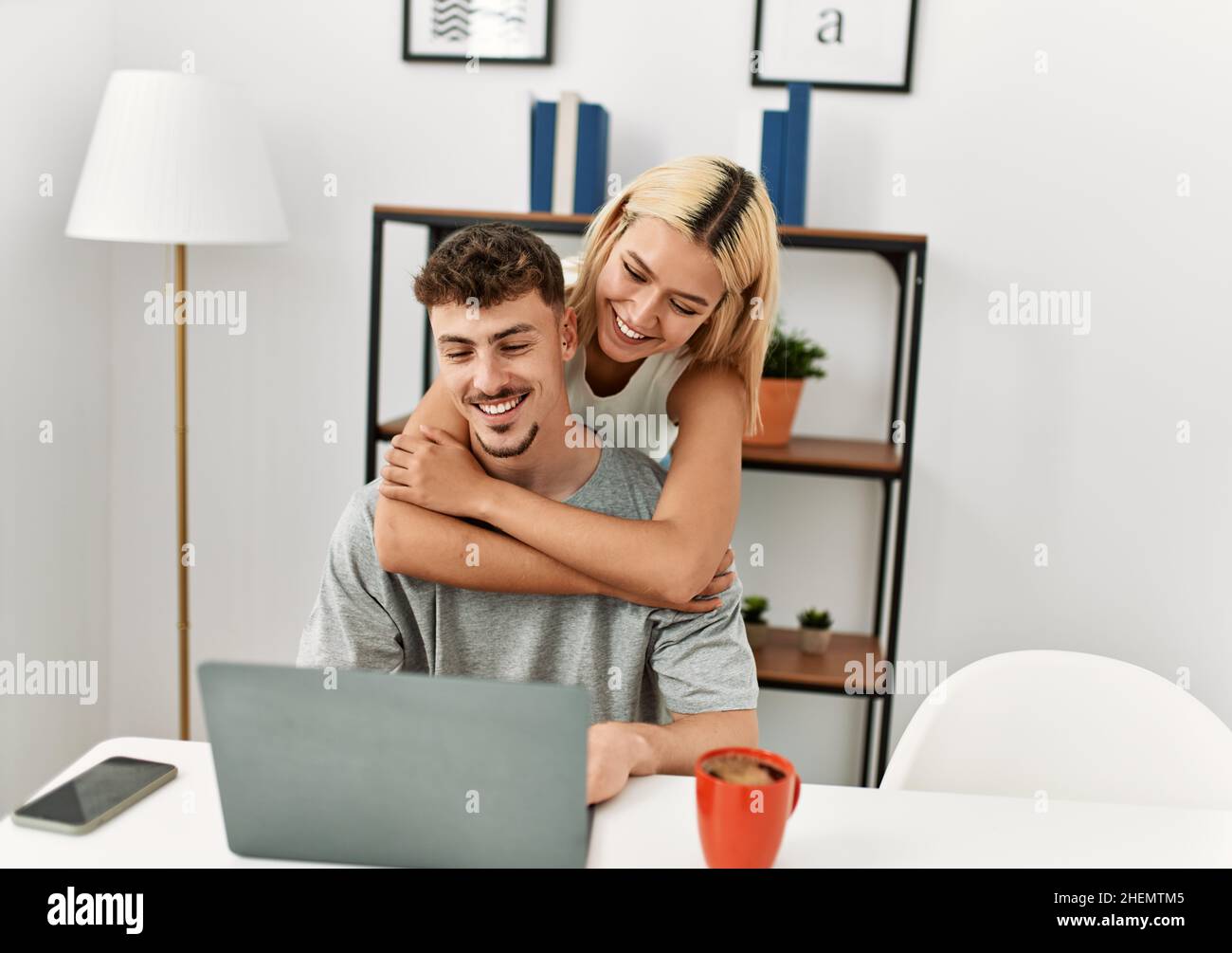 Young caucasian couple hugging and using laptop sitting on the desk at ...