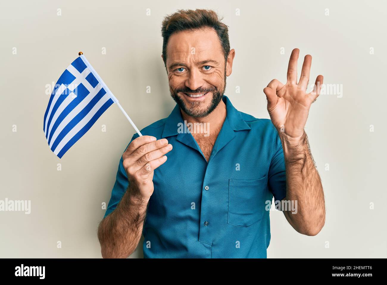 Middle age man holding greece flag doing ok sign with fingers, smiling ...