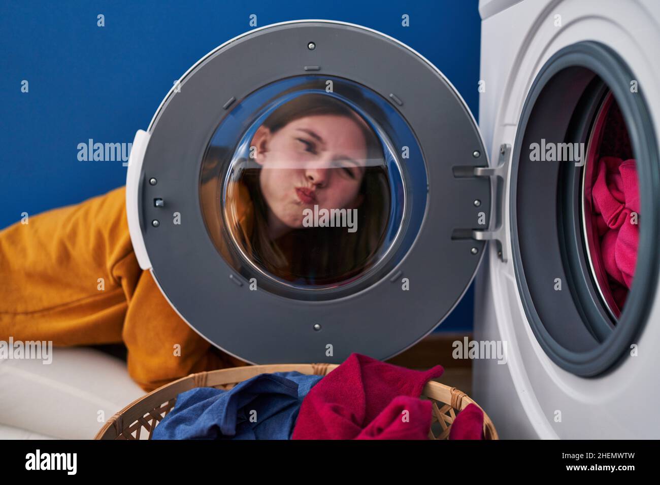 Young brunette woman looking through the washing machine window puffing ...