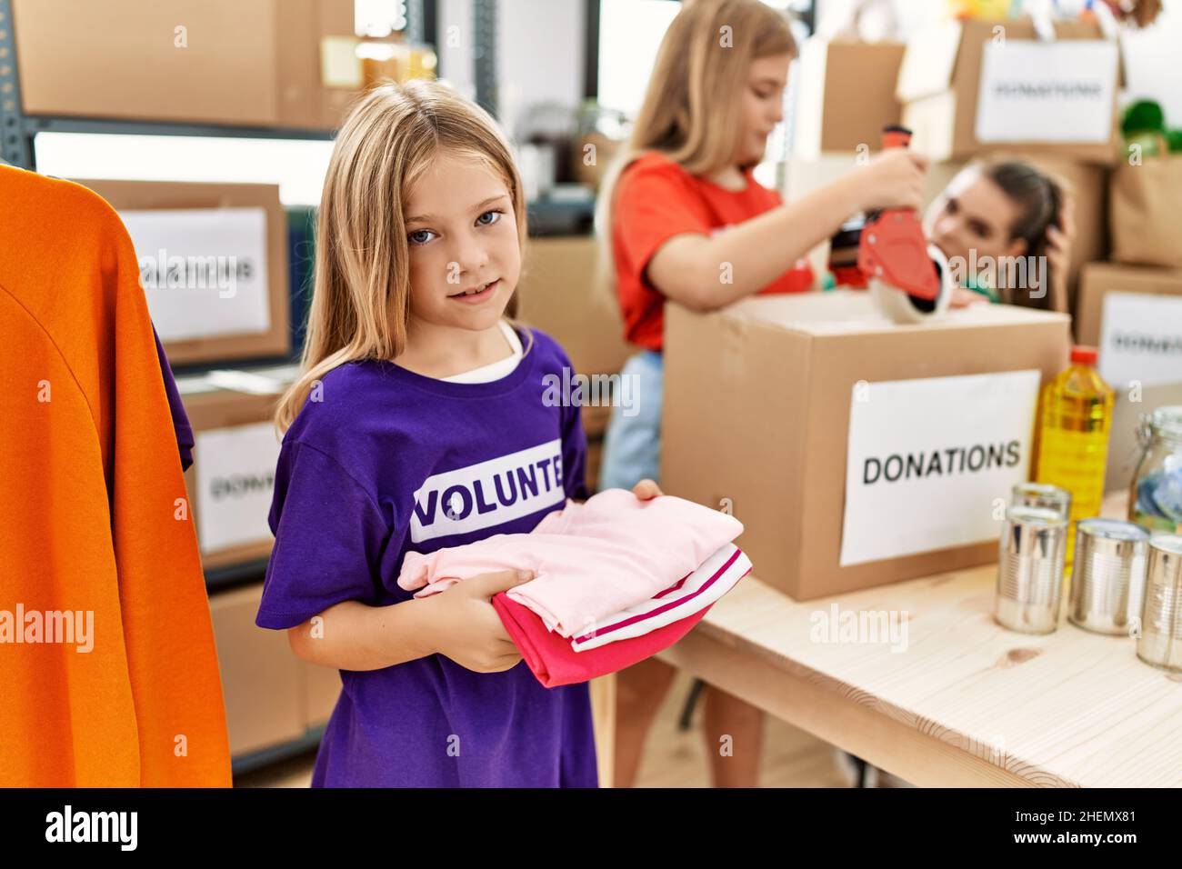 Mother and daughters wearing volunteer uniform holding folded clothes ...
