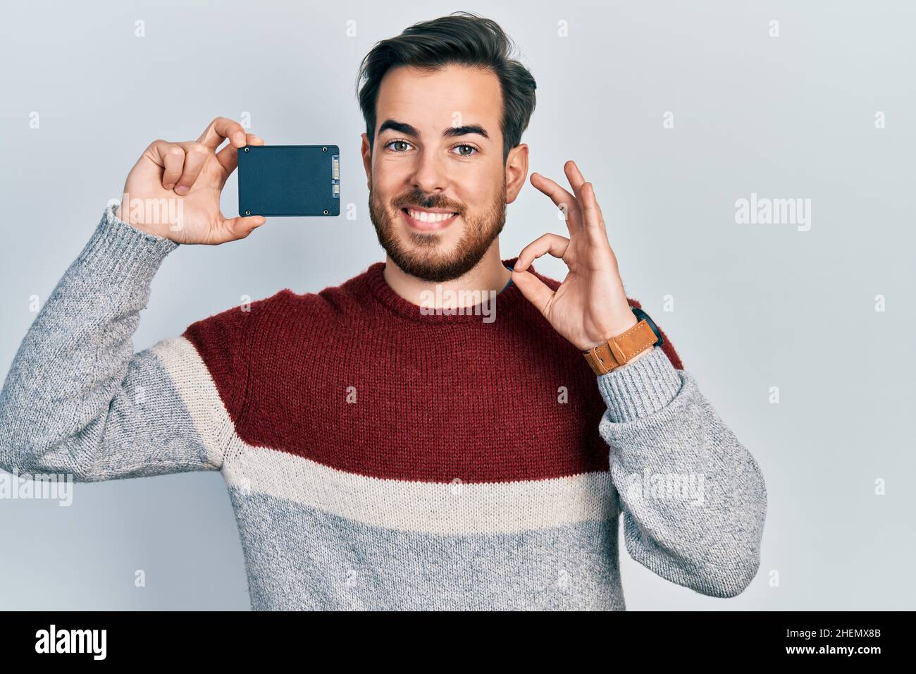 Handsome caucasian man with beard holding ssd memory doing ok sign with ...