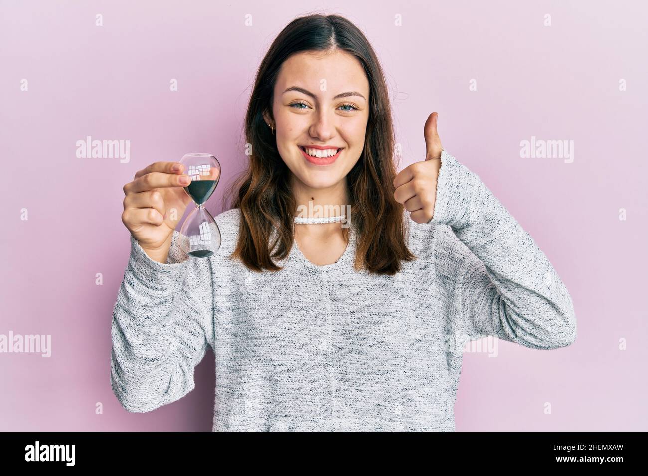Young brunette woman holding sand clock smiling happy and positive ...