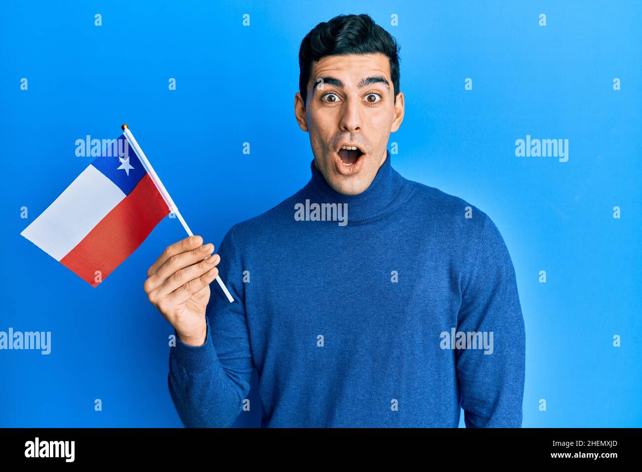 Handsome hispanic business man holding chile flag scared and amazed ...