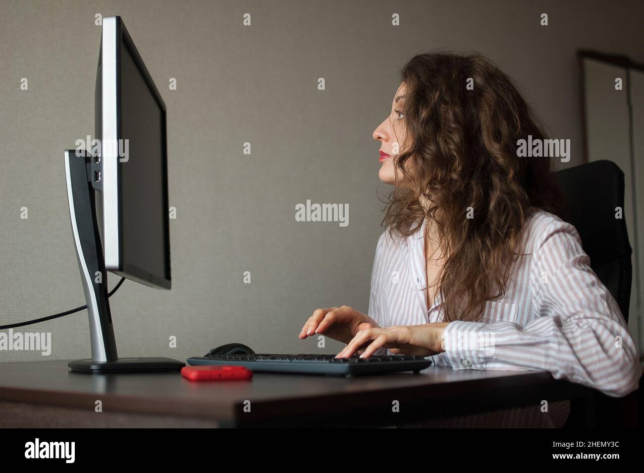 Young female office manager in white shirt and curly hair is sitting at ...