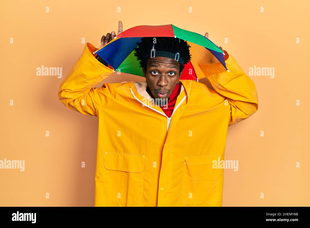 Young african american man wearing yellow raincoat doing funny gesture ...