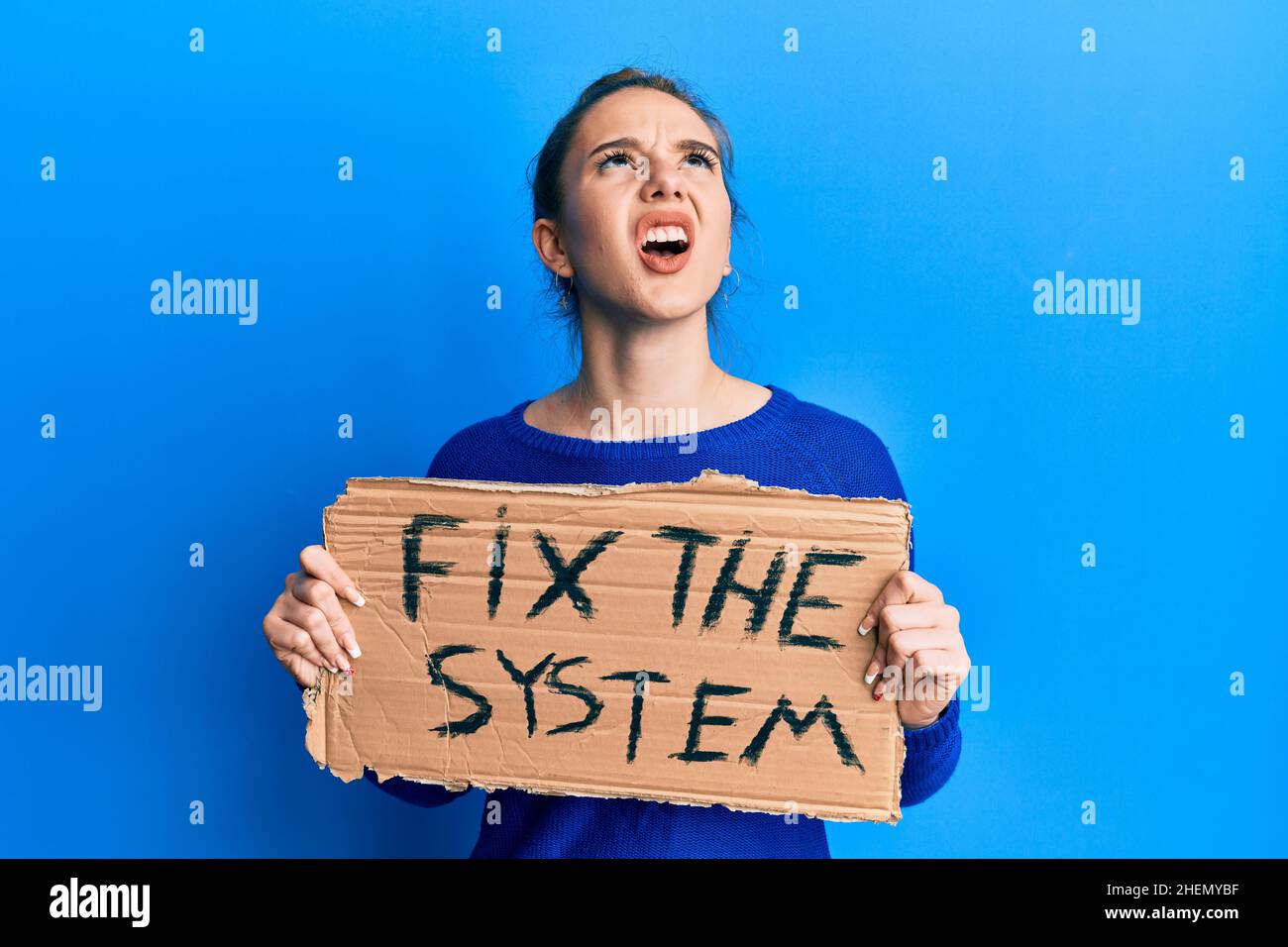Young blonde woman holding fix the system banner cardboard angry and ...
