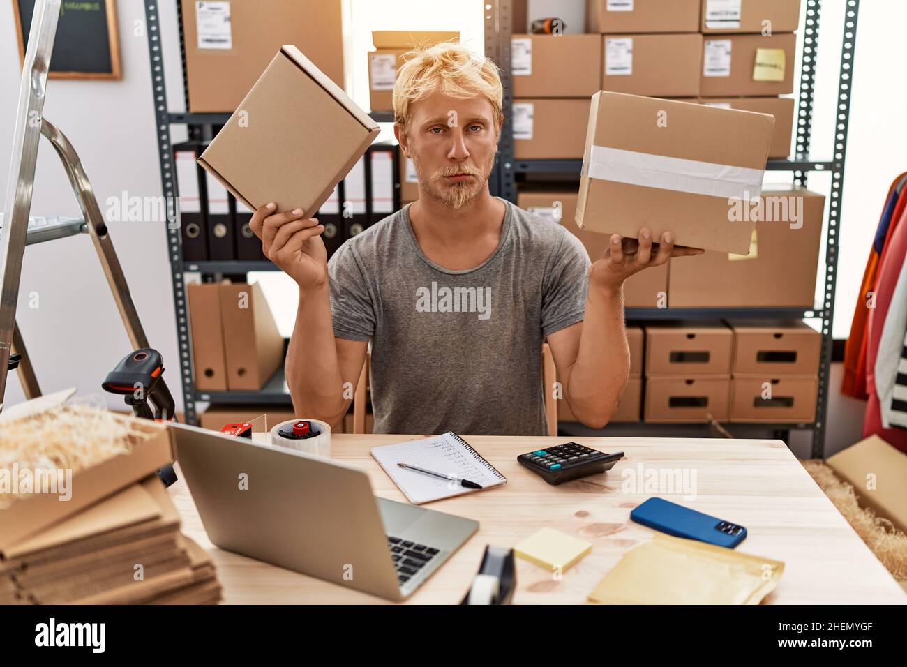 Young blond man holding packages working at online shop depressed and ...