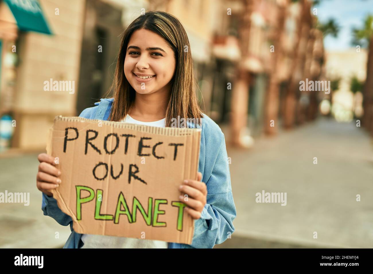 Young latin girl smiling happy holding protect our planet banner at the ...