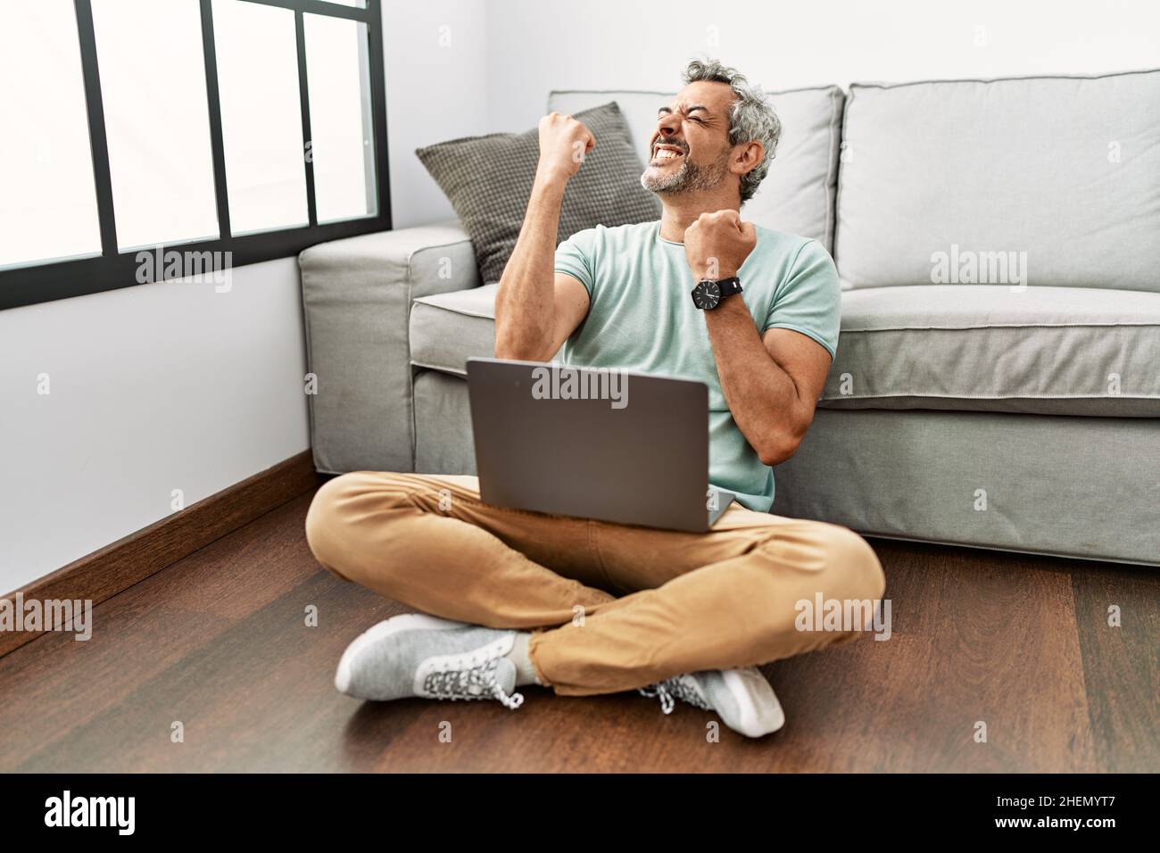 Middle age hispanic man using laptop sitting on the floor at the living ...