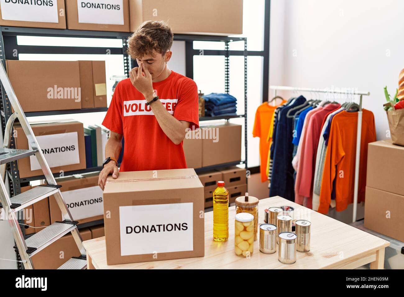 Young caucasian man volunteer holding donations box tired rubbing nose ...