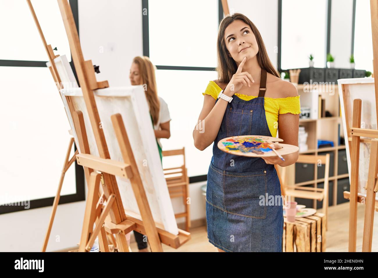 Young hispanic woman at art classroom serious face thinking about ...