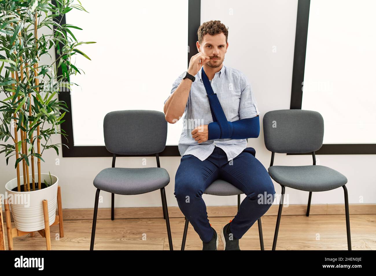 Handsome young man sitting at doctor waiting room with arm injury mouth ...
