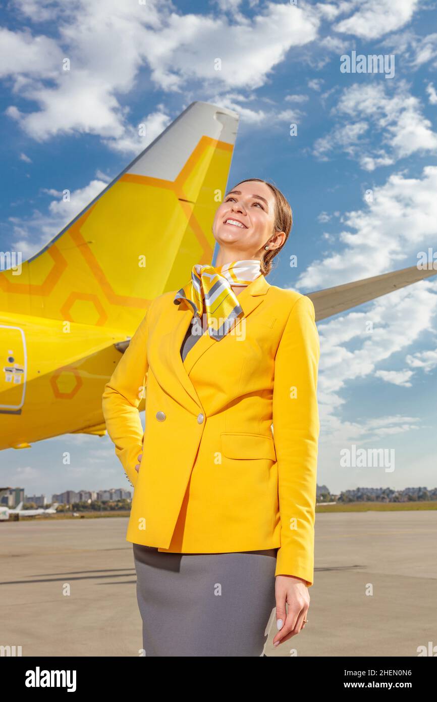 Cheerful stewardess in airline uniform looking at sky and smiling while ...