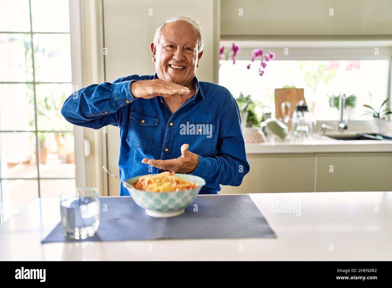 Senior man with grey hair eating pasta spaghetti at home gesturing with ...