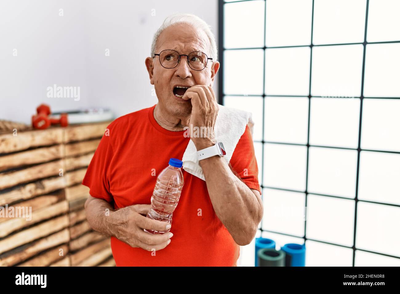 Senior man wearing sportswear and towel at the gym looking stressed and ...