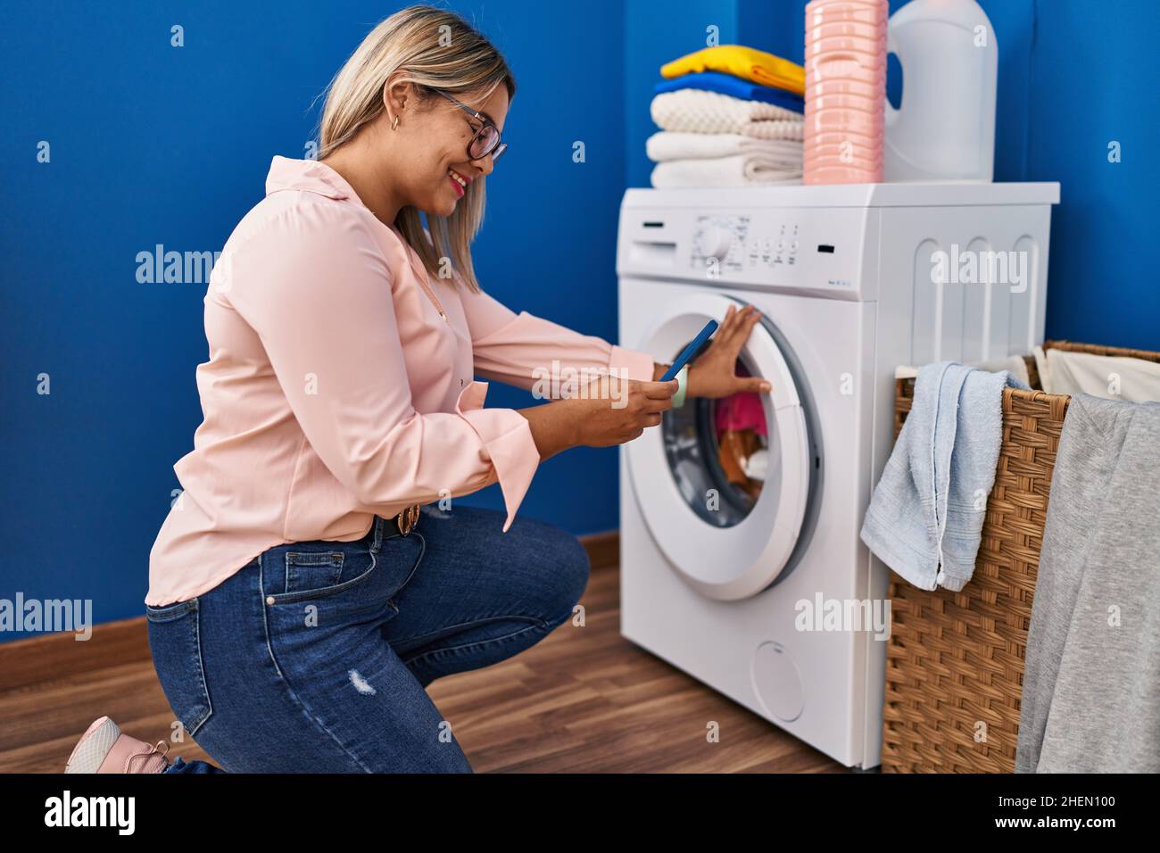 Young hispanic woman using smartphone waiting for washing machine at ...