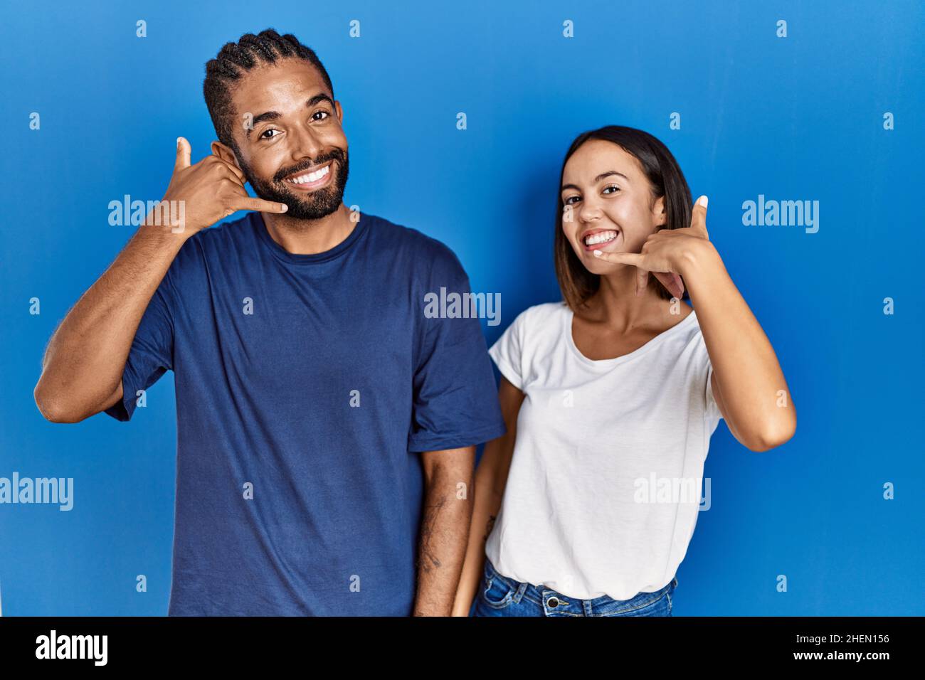 Young hispanic couple standing together smiling doing phone gesture ...
