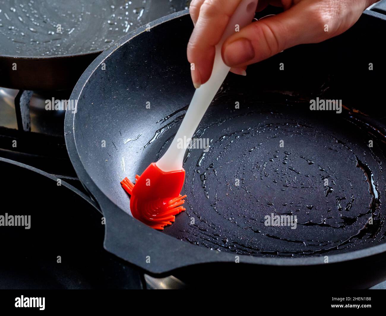 Human hand oiling a red-hot pan with a red silicone kitchen brush ...