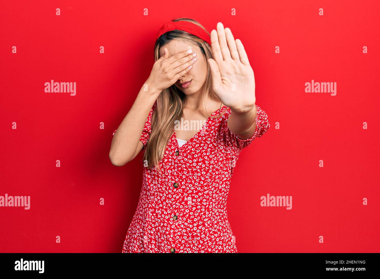 Beautiful hispanic woman wearing summer dress covering eyes with hands ...
