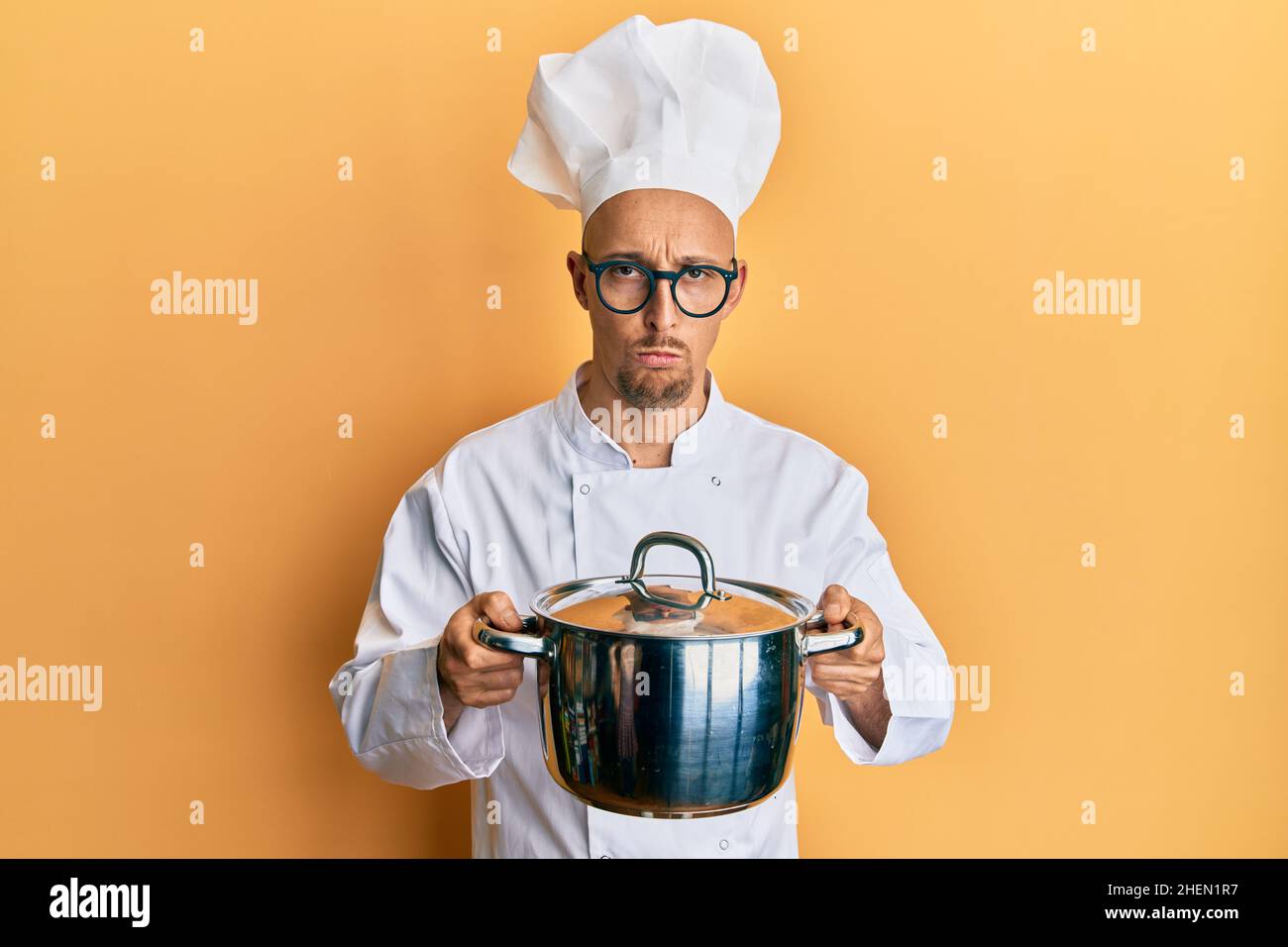 Bald man with beard wearing professional cook holding cooking pot ...
