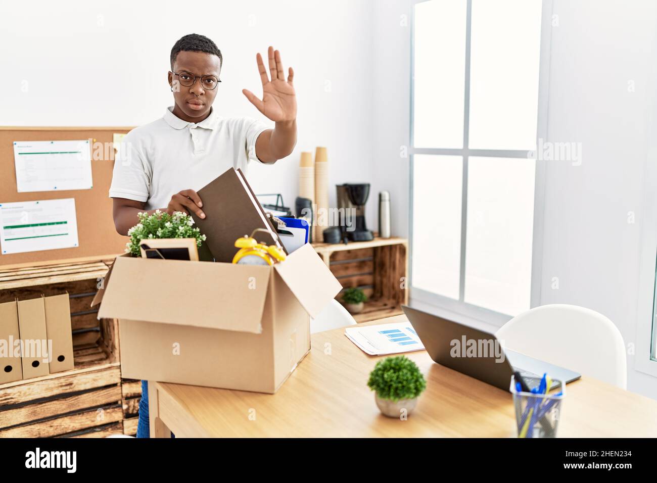 Young african man putting office objects into cardboard box with open ...