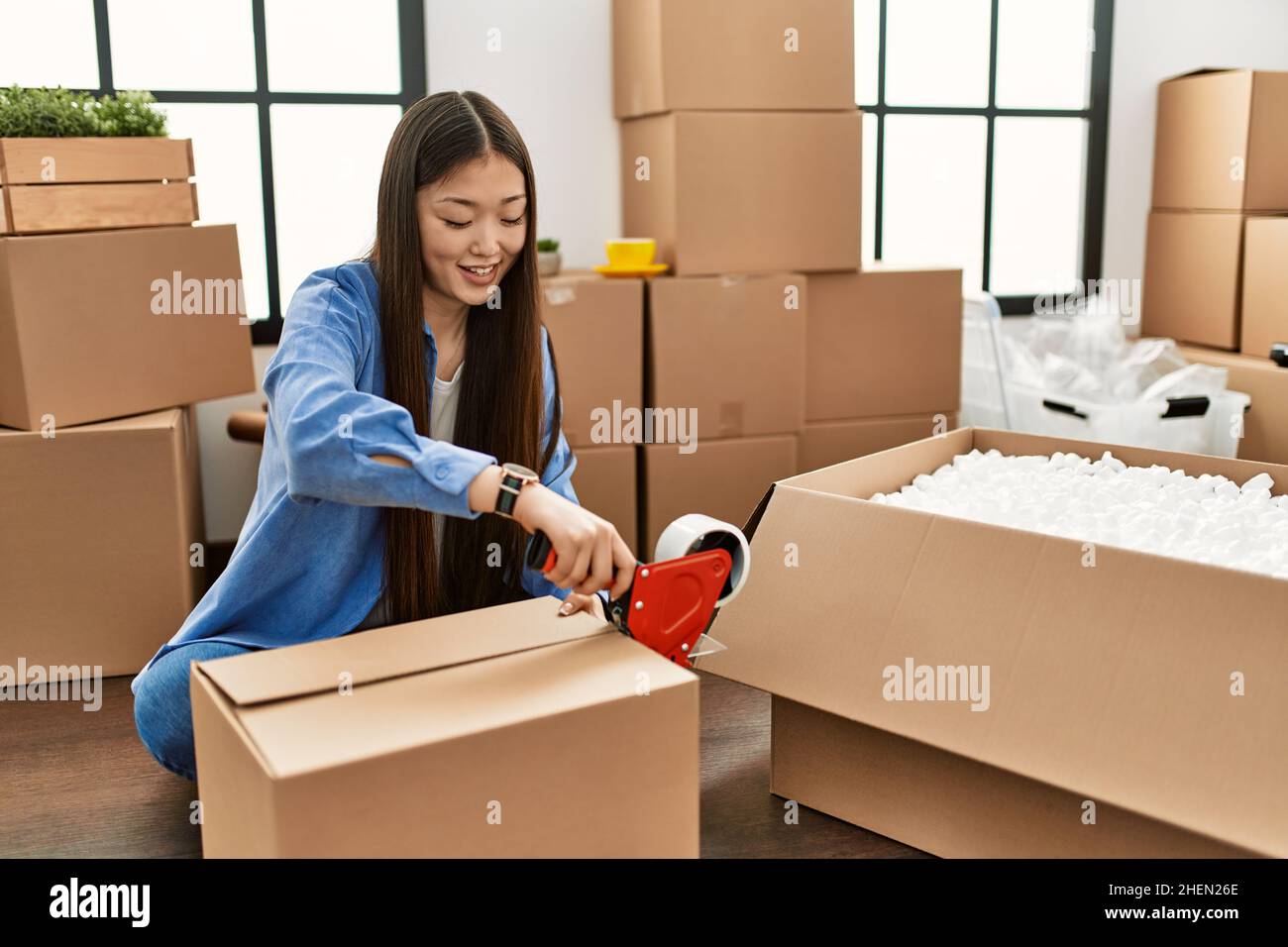 Young chinese girl smiling happy closing box using packing tape at new ...