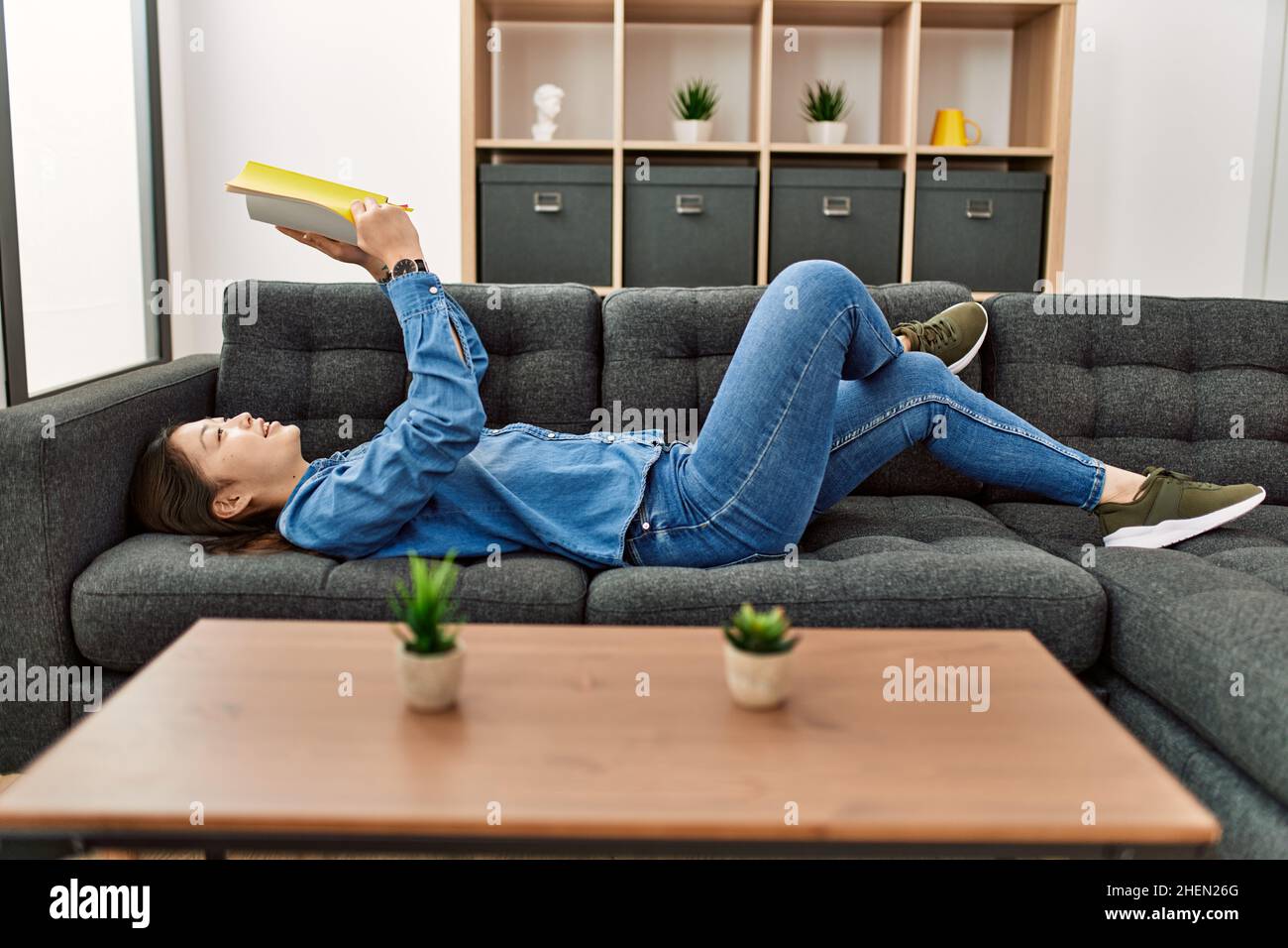Young chinese girl reading book lying on the sofa at home Stock Photo ...