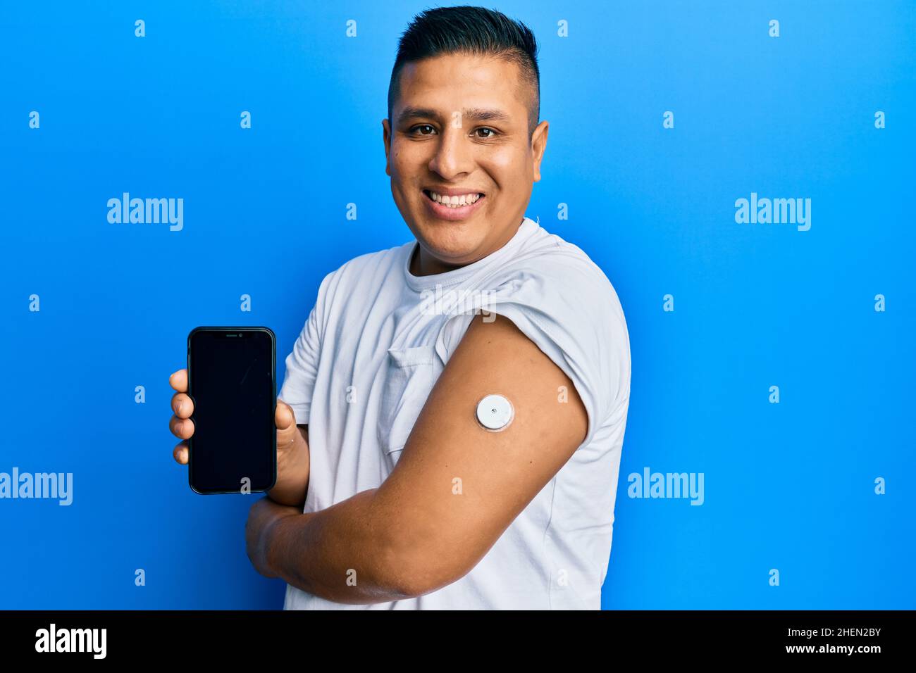 Hispanic man showing diabetes device on arm and holding smartphone with ...