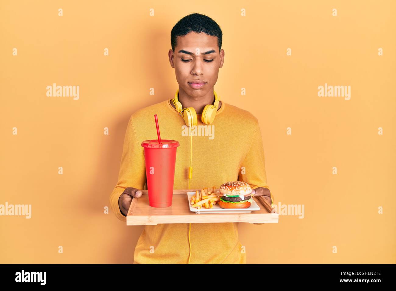 Young african american guy eating a tasty classic burger depressed and ...