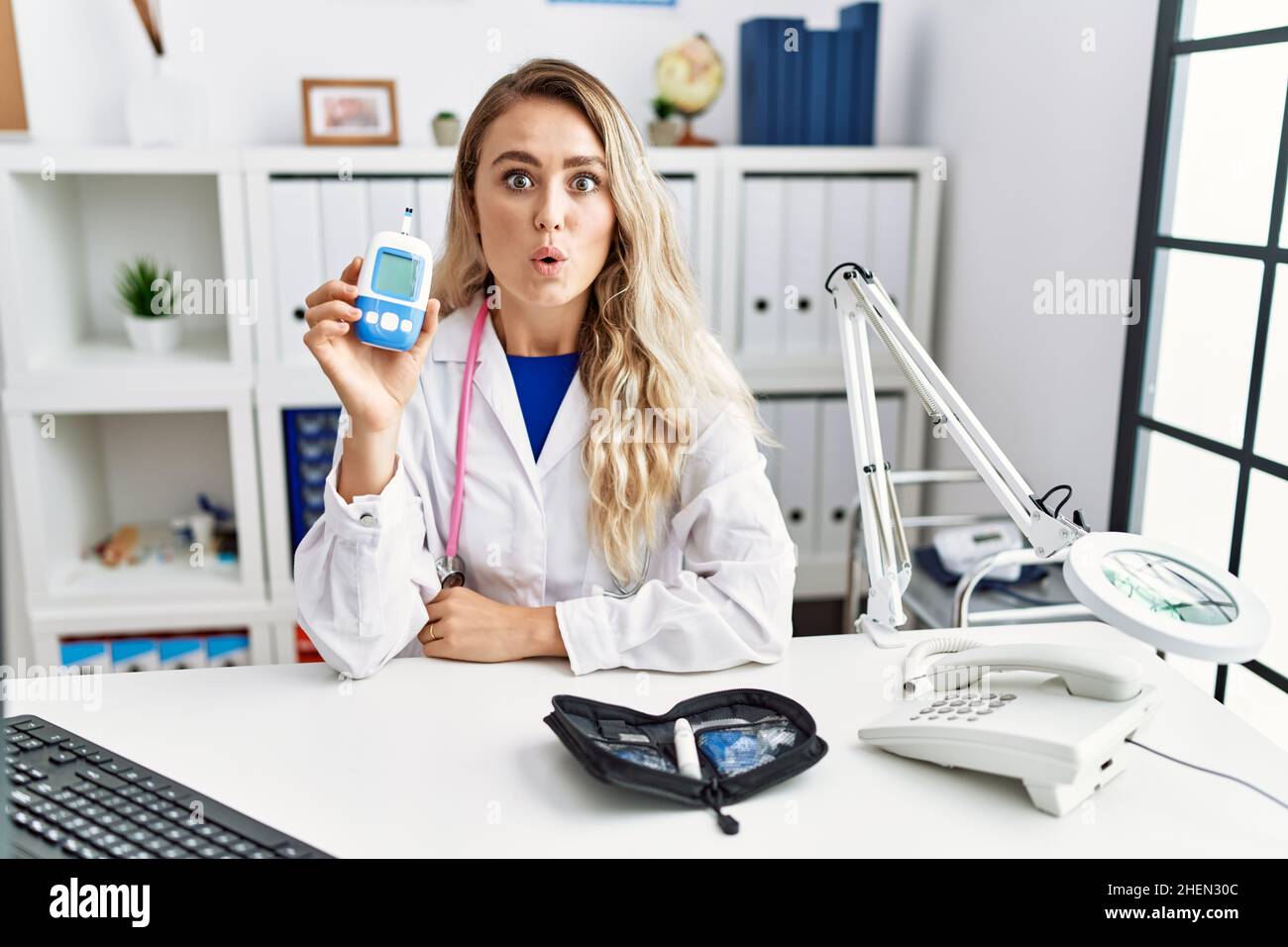Young beautiful doctor woman holding glucose meter scared and amazed ...