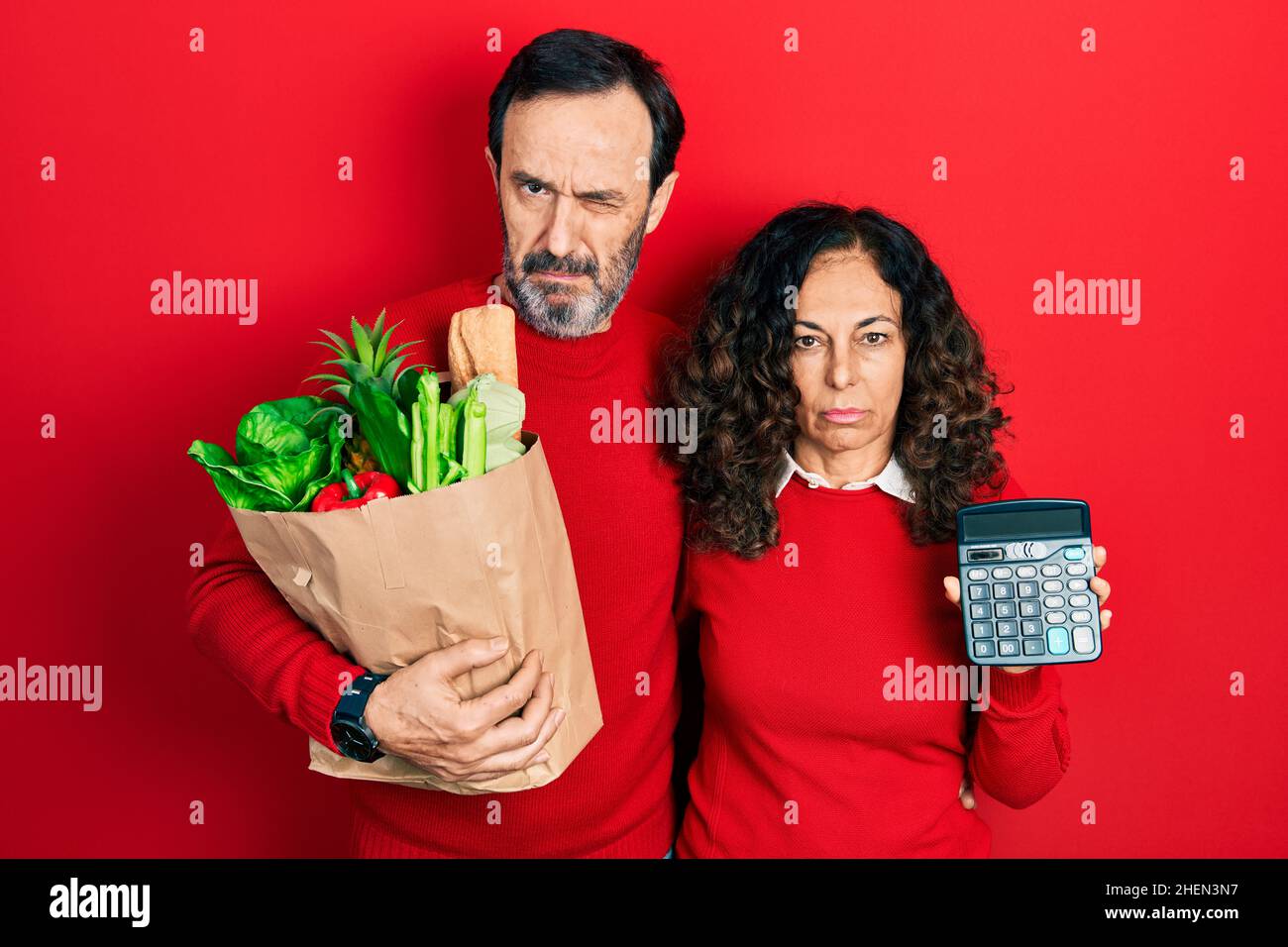 Middle age couple of hispanic woman and man holding groceries bag and ...