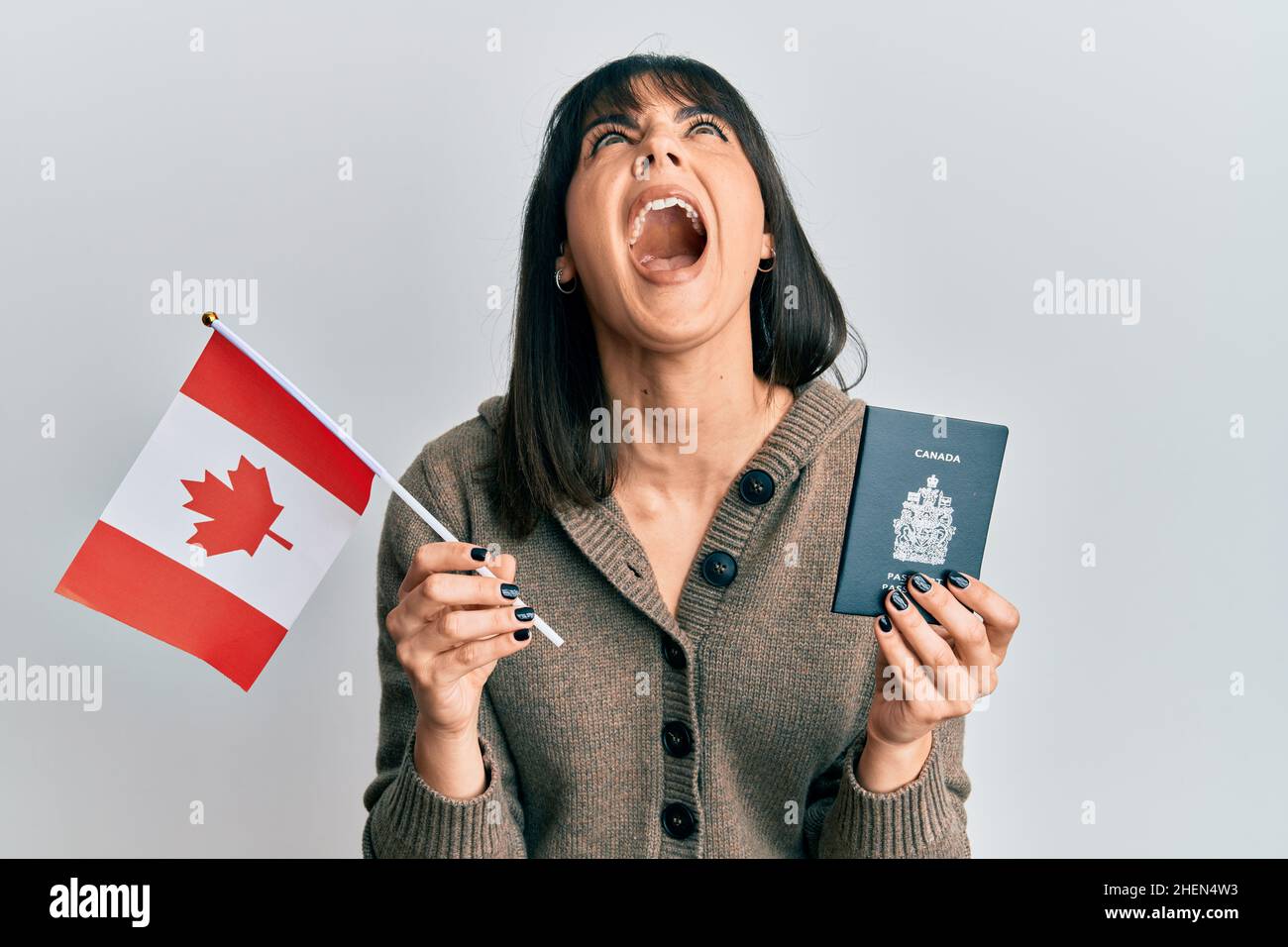 Young hispanic woman holding canada flag and passport angry and mad ...