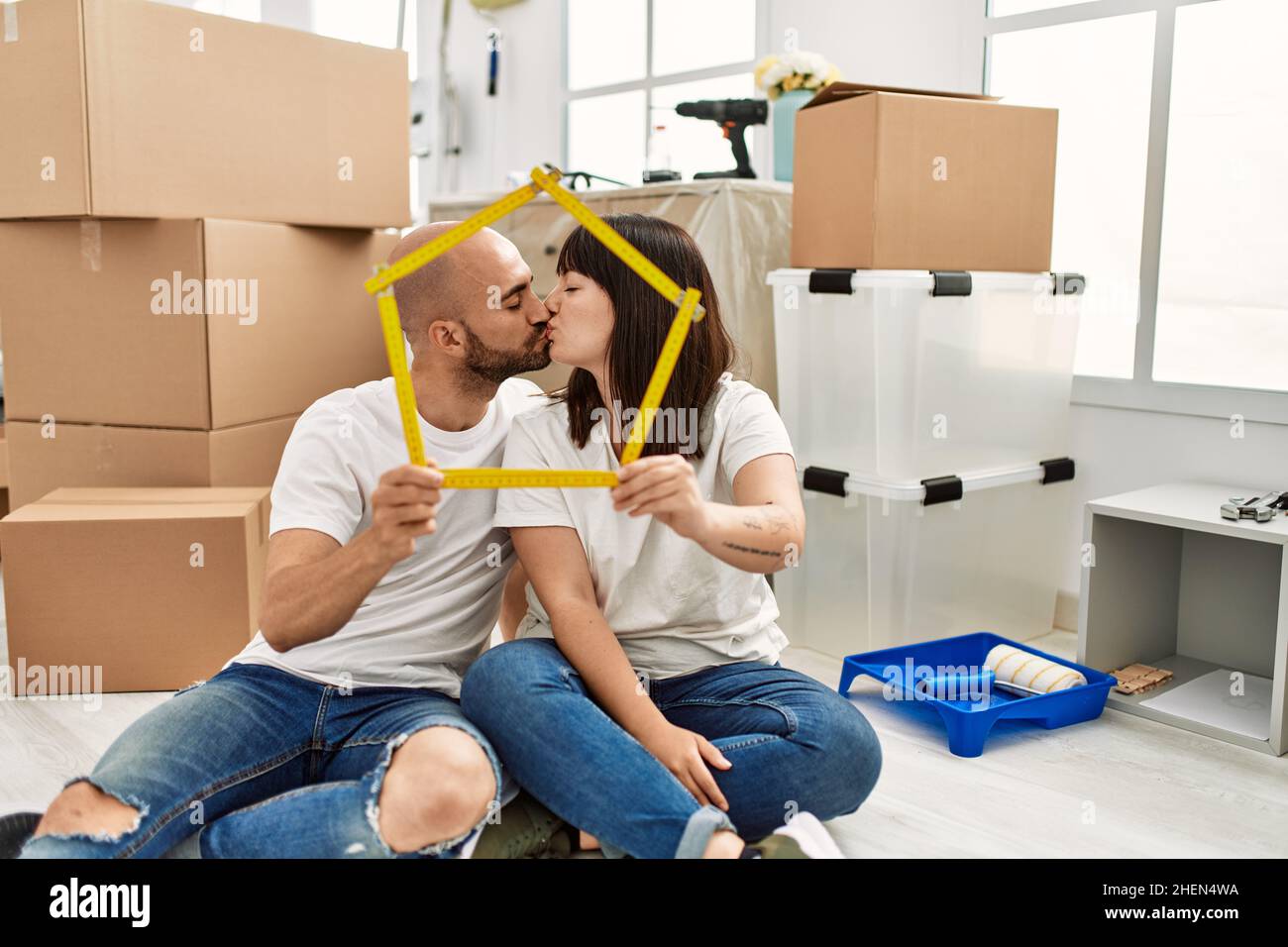 Young hispanic couple kissing and holding house project at new home ...