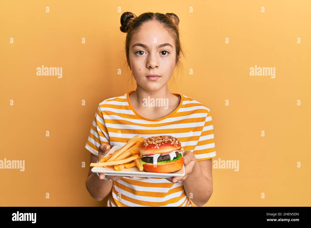 Beautiful brunette little girl eating a tasty classic burger with fries ...