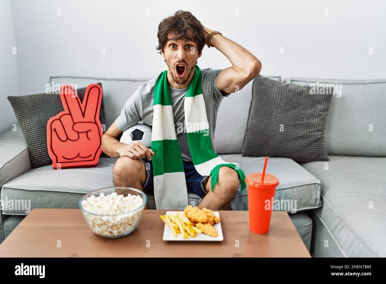 Young hispanic man football hooligan cheering game at home crazy and ...