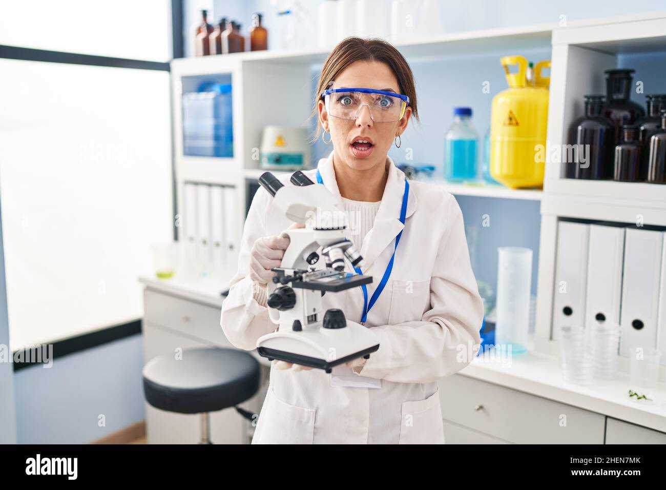 Young brunette woman working at scientist laboratory with microscope in ...