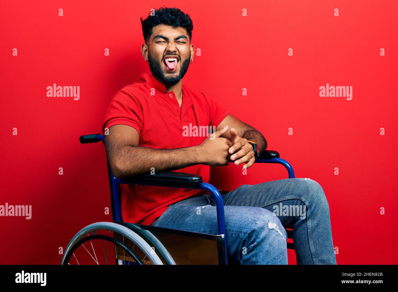 Arab man with beard sitting on wheelchair sticking tongue out happy ...