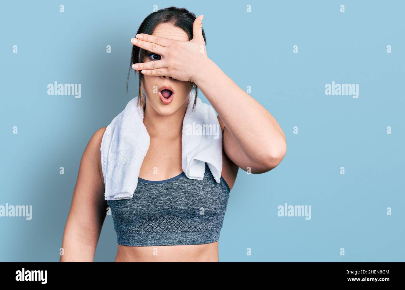 Young hispanic girl wearing sportswear and towel peeking in shock ...